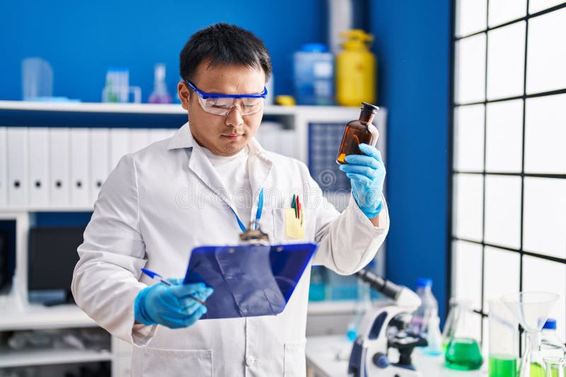 Young Chinese Man Wearing Scientist Uniform Reading Clipboard at ... Young Chinese Man Wearing Scientist Uniform Reading Clipboard at ...