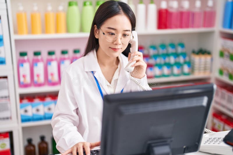 Young Chinese Woman Pharmacist Talking on Telephone Using Computer at ...