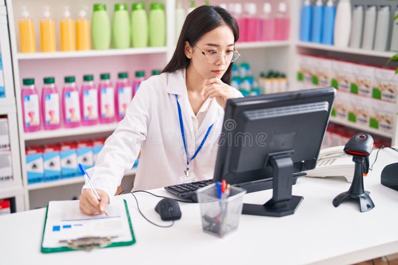 Young Chinese Woman Pharmacist Writing on Document Using Computer at ...