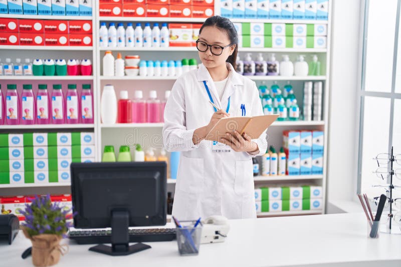 Young Chinese Woman Pharmacist Writing on Notebook Using Computer at ...
