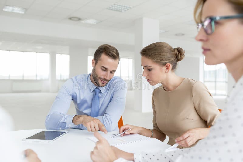Young Colleagues Discussing Over Document at Table during Meeting in ...