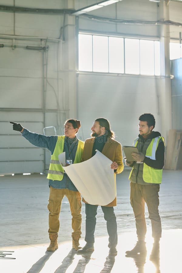 Young Confident Male Engineer Pointing at Wall of Warehouse during ...