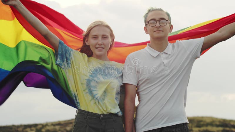 A Young Couple Holds Hands And Raises A Rainbow Lgbt Flag While Looking