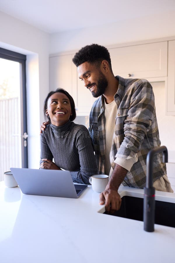Young Couple at Home Looking at Laptop on Counter in Kitchen Together ...