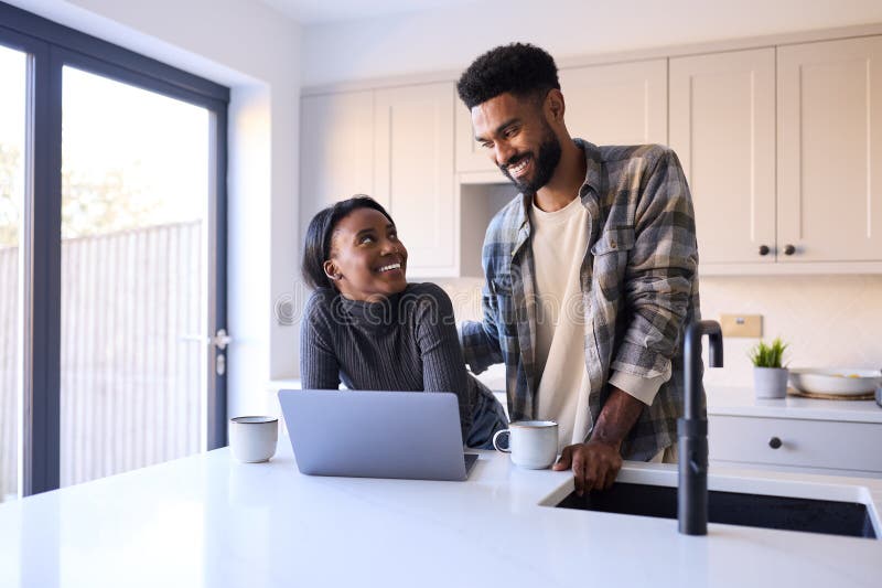Young Couple at Home Looking at Laptop on Counter in Kitchen Together ...