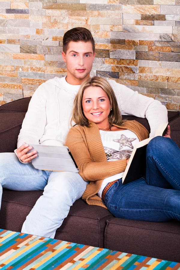 Young Couple at Home, Reading a Book and with a Tablet, Smiling Stock ...
