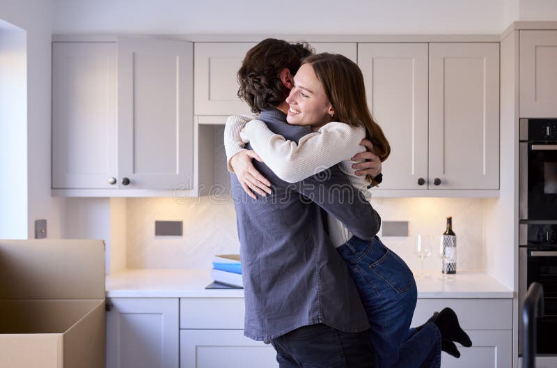 Young Couple Moving into New Home Hugging As they Unpack Boxes in ...