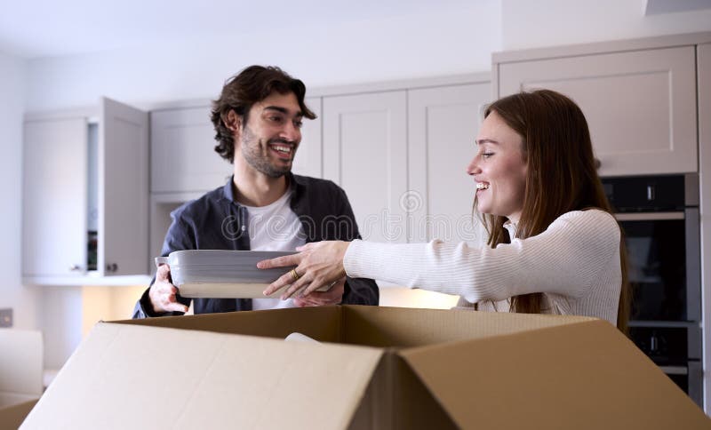 Young Couple Moving into New Home Unpacking Boxes in Kitchen Together ...