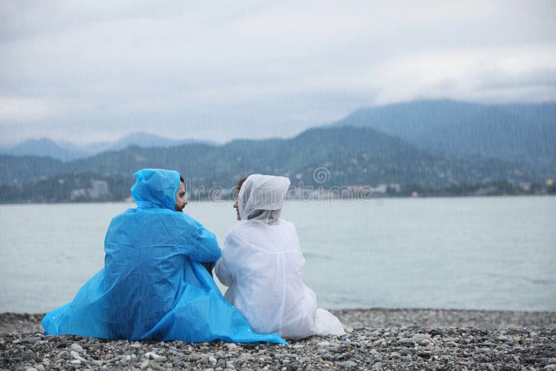 Young Couple in Raincoats Enjoying Time Together Under Rain on Beach ...