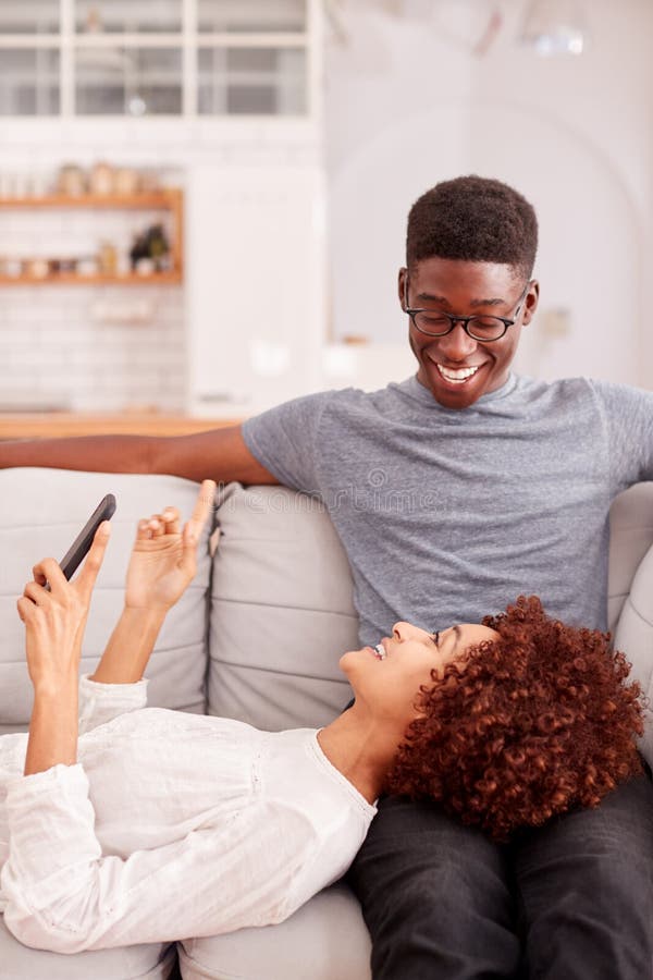 Young Couple Relaxing on Sofa at Home Looking at Mobile Phone Together ...