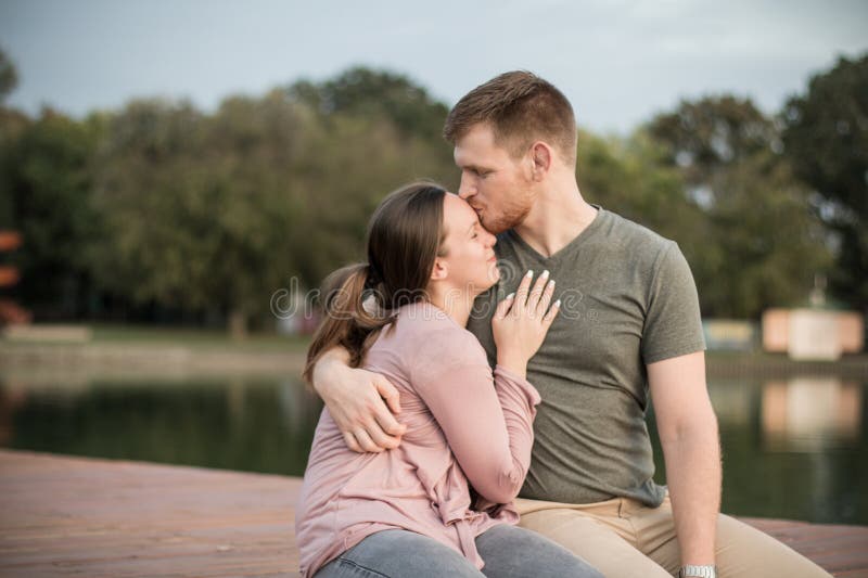Young Couple Sitting On The Dock The Man Kisses The Woman On The