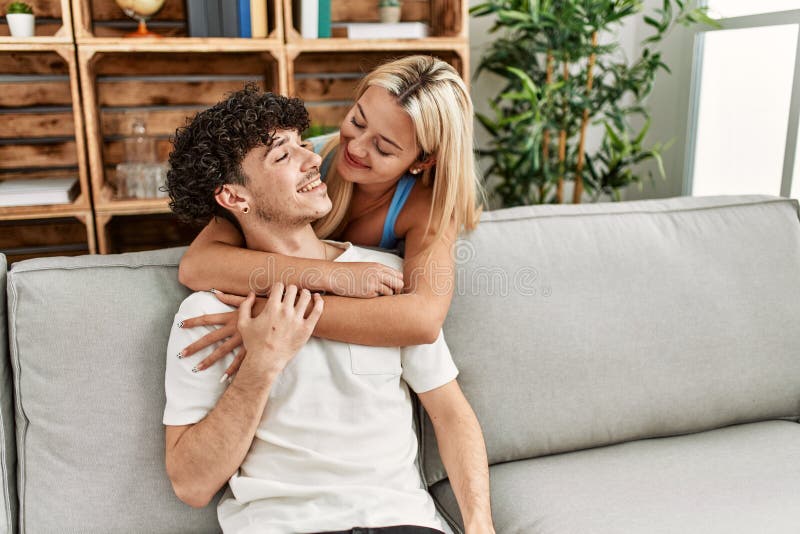 Young Couple Sitting on the Sofa Hugging at Home Stock Photo - Image of ...