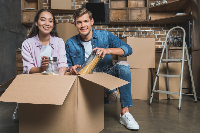 Young Couple Unpacking Boxes on Kitchen while Moving into Stock Image ...