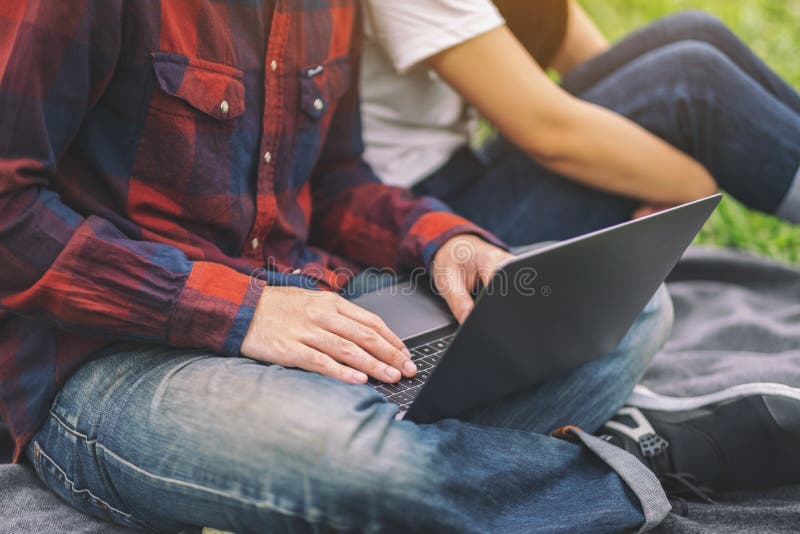 A Young Couple Using Laptop Computer while Sitting in the Park Together ...