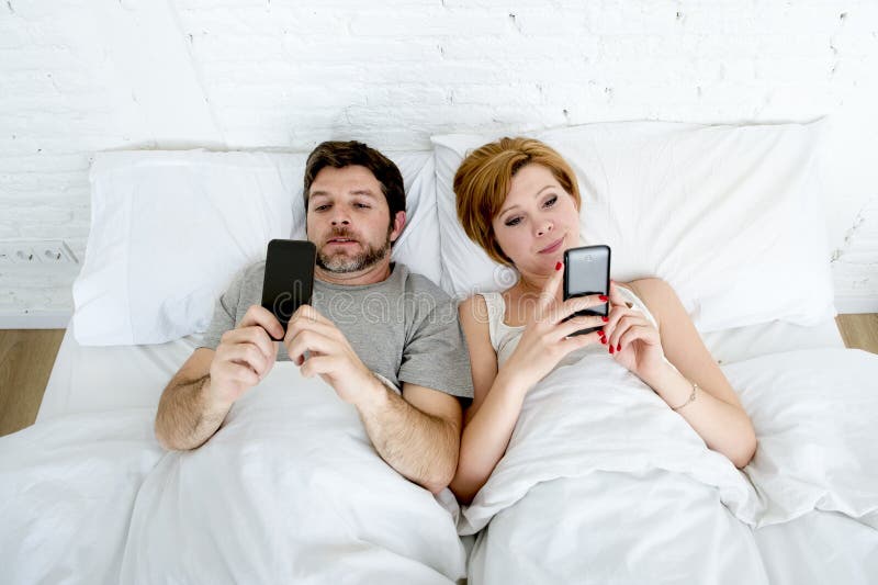 Young Couple Using Mobile Phone in Bed Ignoring Each Other in ...