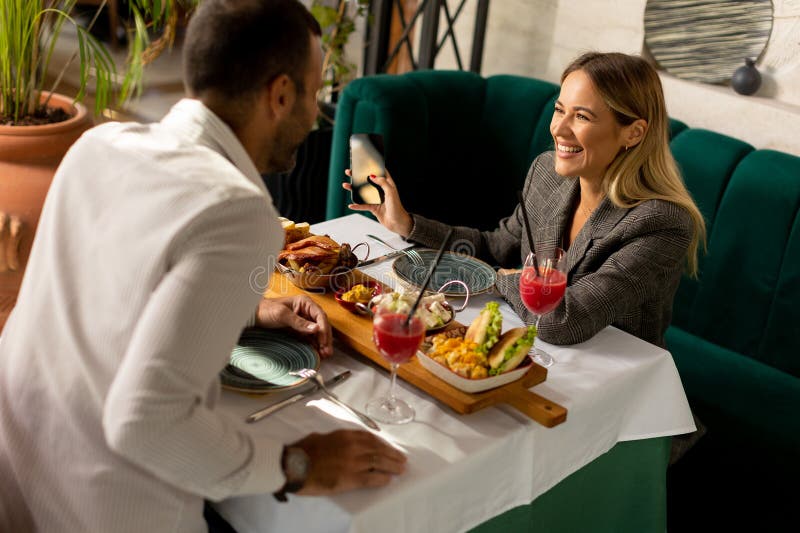 Young Coupleusing Mobile Phone while Having Lunch and Drinking Fresh ...
