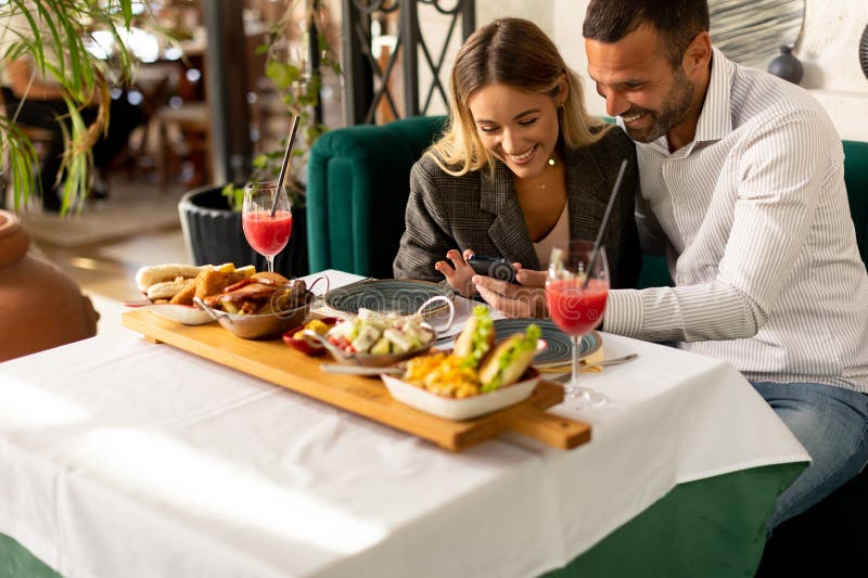 Young Coupleusing Mobile Phone while Having Lunch and Drinking Fresh ...