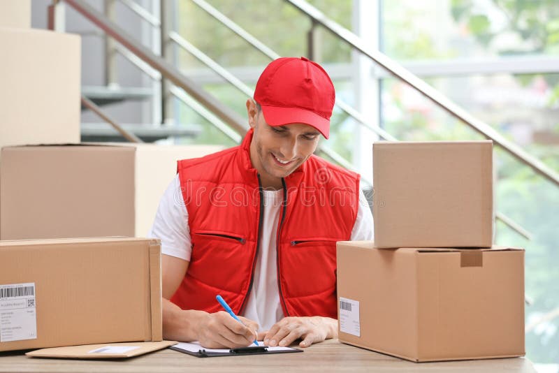Young Courier Working with Papers among Parcels at Table Stock Photo ...