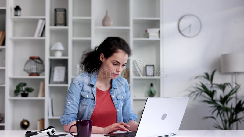 A Young Curly-haired Brunette Student Sits at a Table and Uses a Laptop for Learning. Online ...
