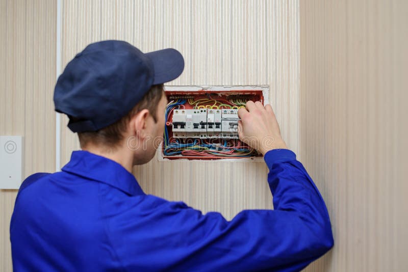 Young Electrician in Blue Overall Disassembling a Electrical Panel ...