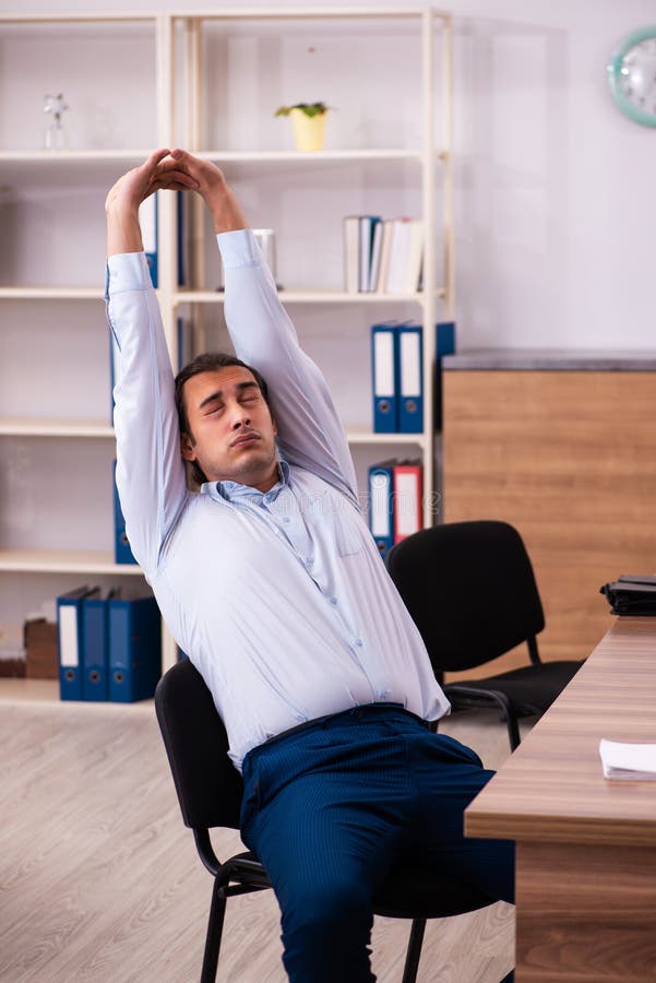 Young Male Employee Stretching at Workplace Stock Image - Image of ...