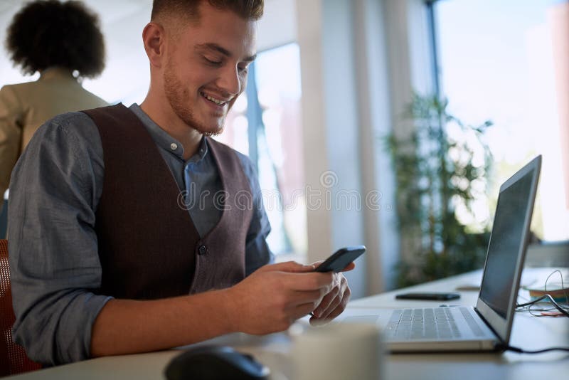 Young Employee Watching His Cell Phone, Smiling, on His Workplace in ...