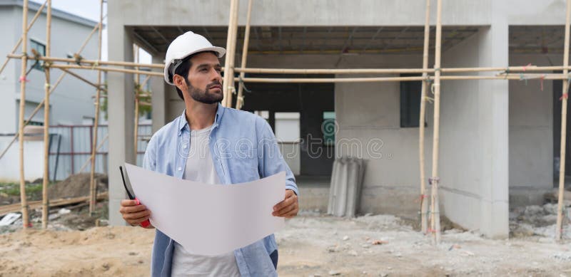 Young Engineer in a Construction Helmet Holding a Floor Plan while ...