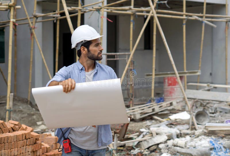 Young Engineer in a Construction Helmet Holding a Floor Plan while ...