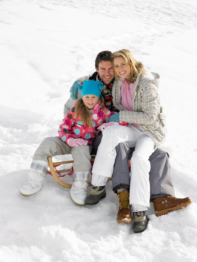 Young Family Sitting on a Sled in the Snow Stock Photo - Image of knee ...