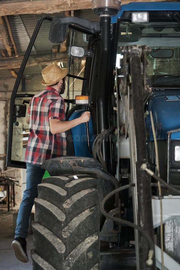 Young Farmer Climbing in a Tractor in a Barn. Stock Photo - Image of ...