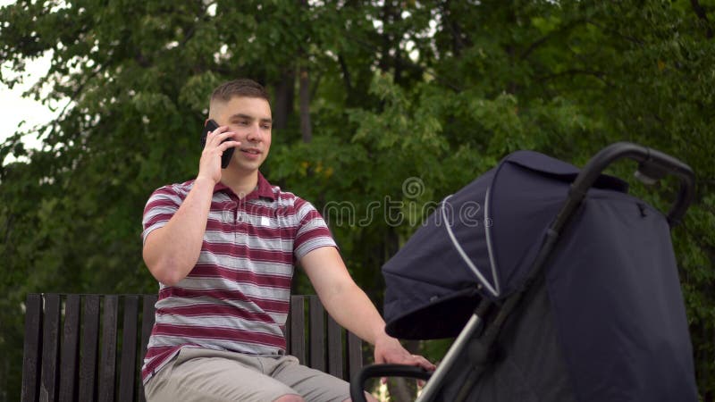 A Young Father is Talking on the Phone and Rocking the Stroller. a Man ...