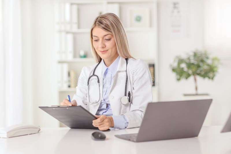 Young Female Doctor Sitting in an Office and Writing a Document at with ...