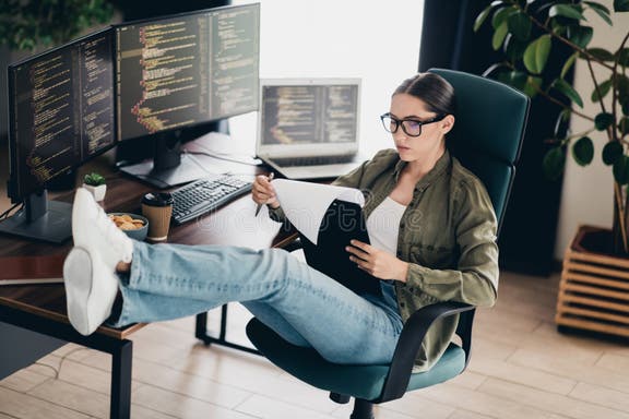 Young Female Programmer Working Remotely at Her Workspace with Monitors, Coding Software, and ...