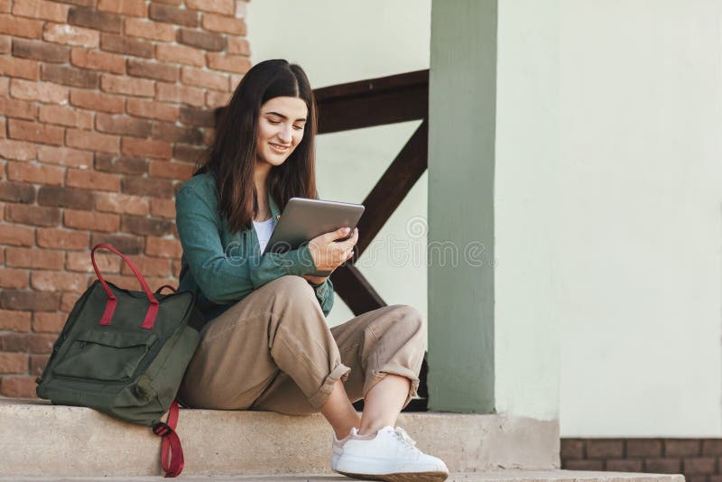 Young Female Student Sitting on Steps and Studying with Tablet in ...