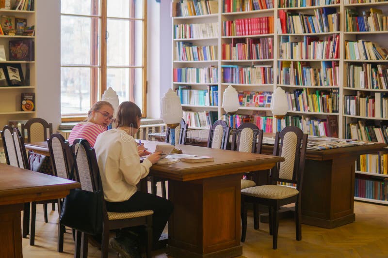 Young Female Students Sitting at a Table in a Library and Reading a ...