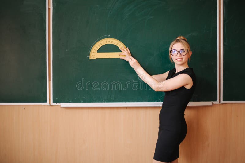 Young Female Teacher In Glasses Stand In Front Of Blackboard Stock