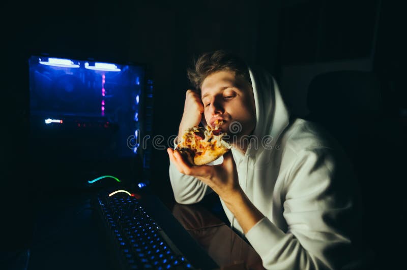 Young Gamer Sits At Home At The Table At The Computer And Eats Pizza ...