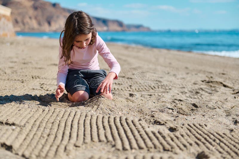Young Girl Creating Patterns in the Sand at a Serene Beach Setting ...