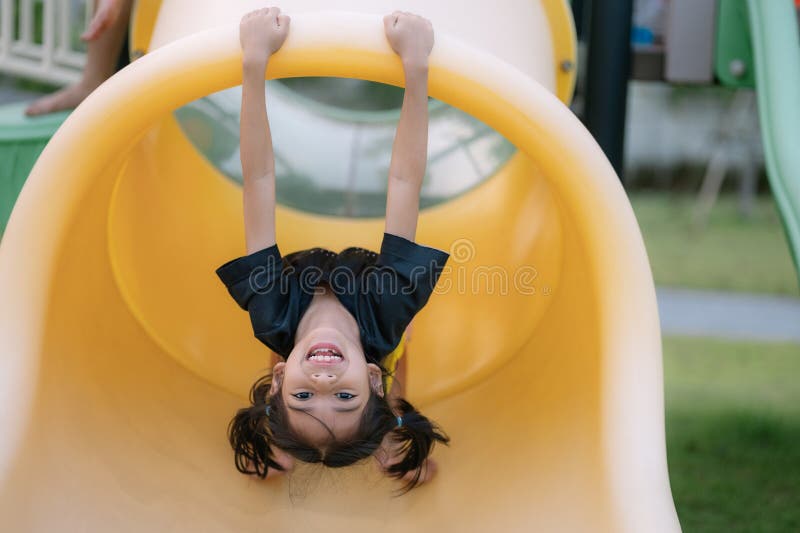 A Young Girl is Hanging Upside Down on a Yellow Slide Stock Image ...