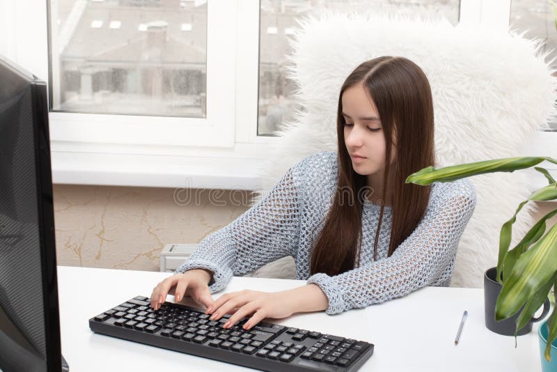 Young Girl Sits at a Table, Typing on a Computer, Smiling Stock Image ...