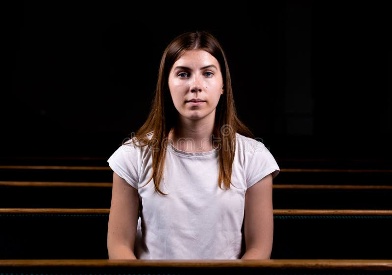 A Young Girl is Sitting Alone in a Large Hall Looking at the Camera ...
