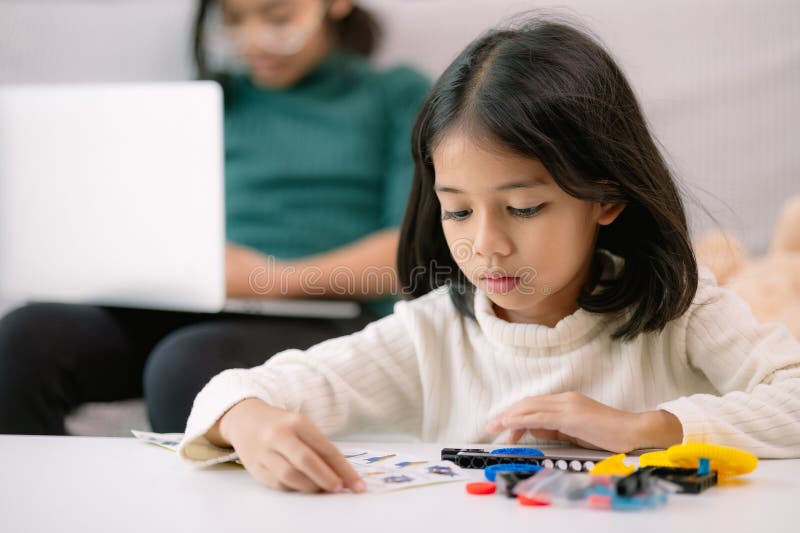 A Young Girl is Sitting at a Table with a Laptop and a Stack of Legos ...
