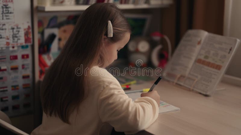 Young Girl Writing in Notebook at Desk, Focused on Studying Stock ...