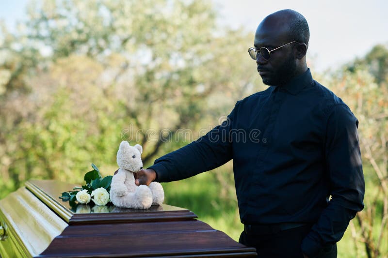 Young Grieving African American Man Putting Teddybear On Closed Lid Of