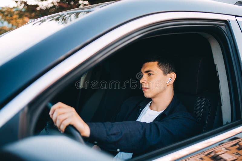 A Young Guy Behind the Wheel of a Car Will Use Wireless Headphones ...