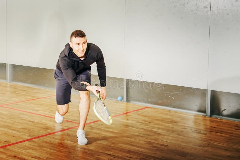 Young Guy Playing a Squash Game. Man Holding a Racket and Kicks the ...