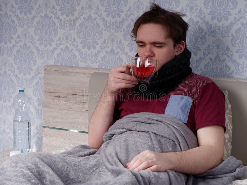 A Young Guy in a Red T-shirt Sits on the Bed and Drinks Tea for a Cold ...