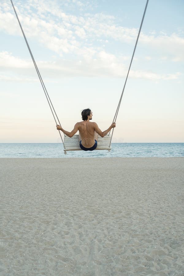 Young Guy on Rope Swing on the Beach on Sea Background. Back View ...