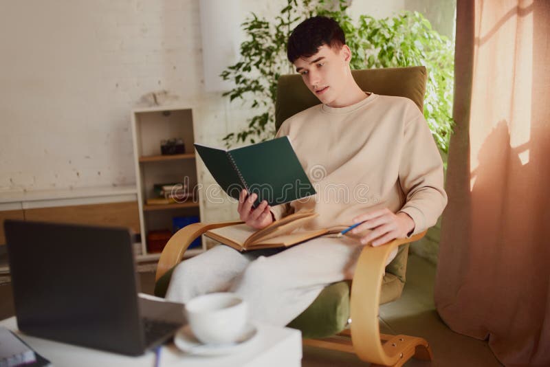 Young Guy, Student Sitting on Chair and Looking on Notes, Doing ...