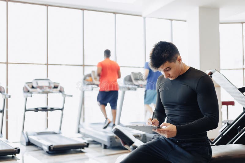 Young Guy Trainer Takes Notes in the Gym. Personal Trainer for Sports ...